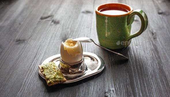 Breakfast on wooden table. Boiled egg in a stand, bread with avocado ...