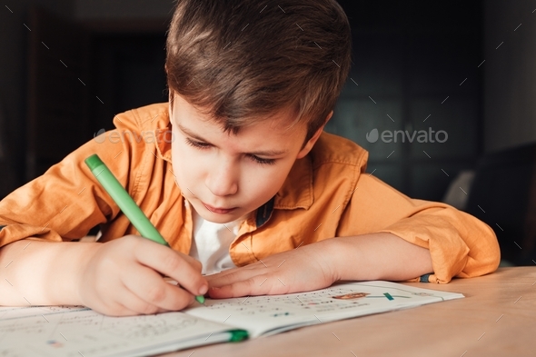 Cute 7 years old child doing his homework sitting by desk Stock Photo ...
