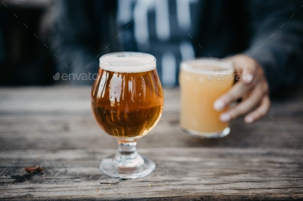 Beer glass sitting on outdoor picnic table at brewery with hands in ...