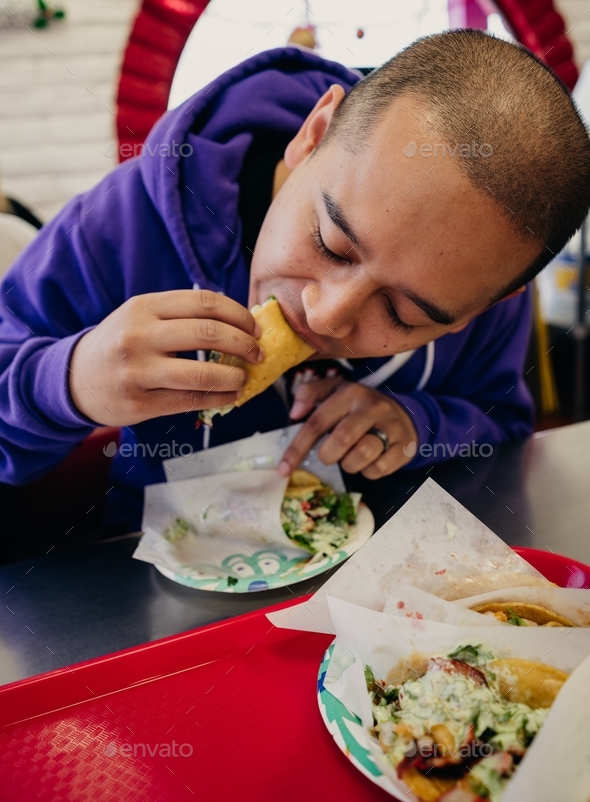 Young man eating biting taco street food Mexican cuisine ethnic diverse ...