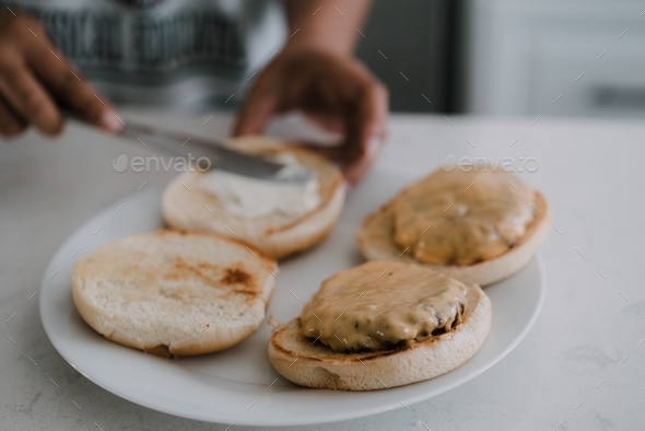 hand spreading mayonnaise onto cheeseburger buns in a kitchen while ...