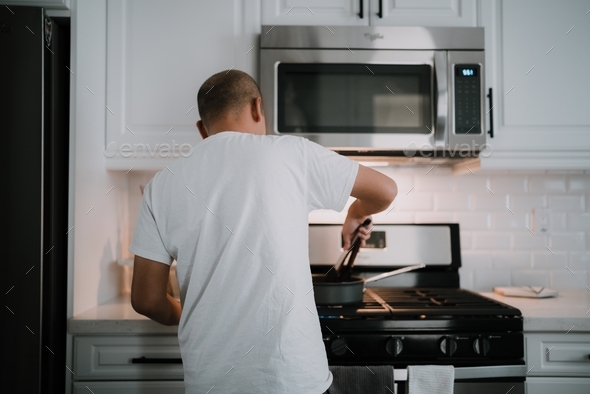 young man cooking in kitchen at home bright pan clean minimal stove ...