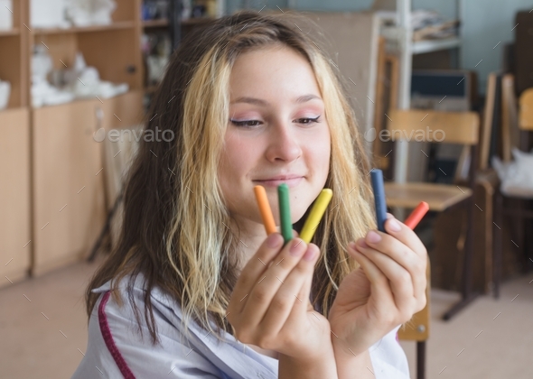 Portrait of a beautiful long-haired teenage girl artist holding crayons ...