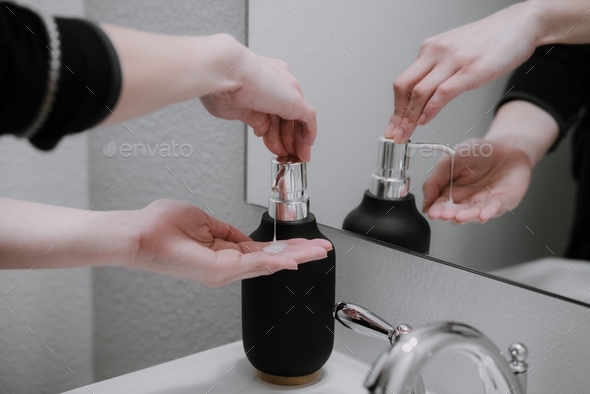 hands using soap pump dispensing to clean hands in bathroom sink next ...