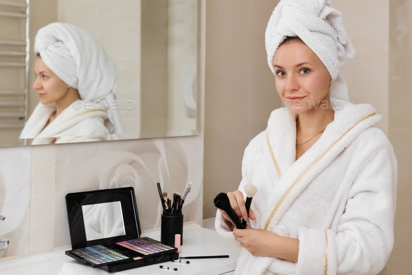 Woman doing herself makeup at home after taking shower. Self skin care ...