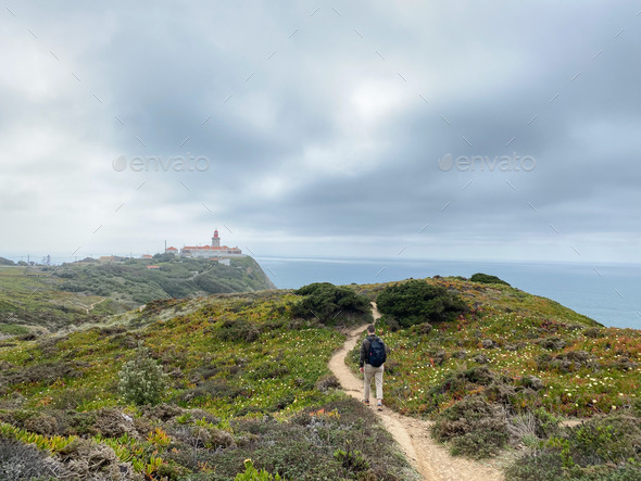 Young man hiking to a lighthouse on the top of the cliff at Cabo da ...