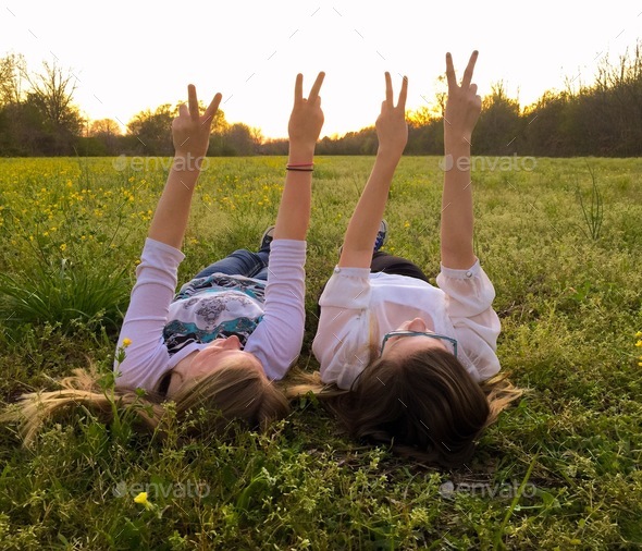 Teenage girls giving peace sign in field at sunset Stock Photo by bwise346