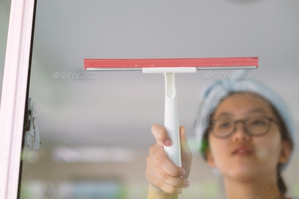 A girl with eyeglasses using wiper to clean a window of her house Stock ...