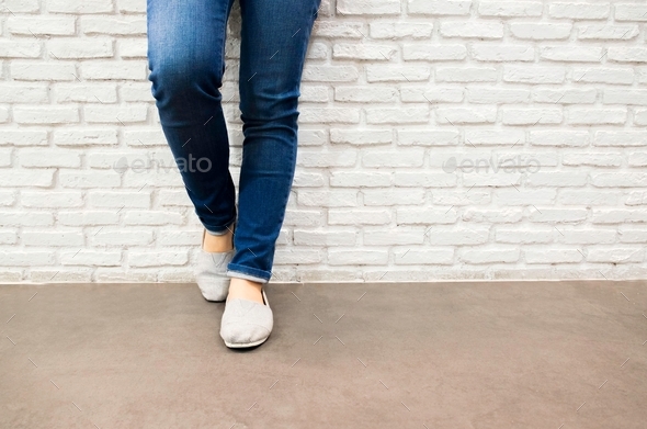 Low section image of woman wearing jean and grey shoes leaning on white ...