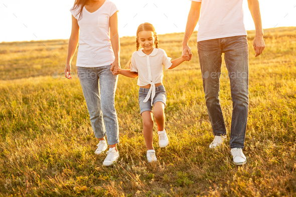 Cheerful daughter walking with anonymous parents in field Stock Photo ...
