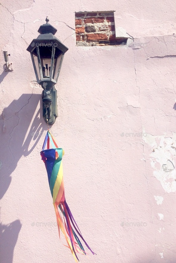 Lamp with a pride pennant flag on a light pink wall in the street ...