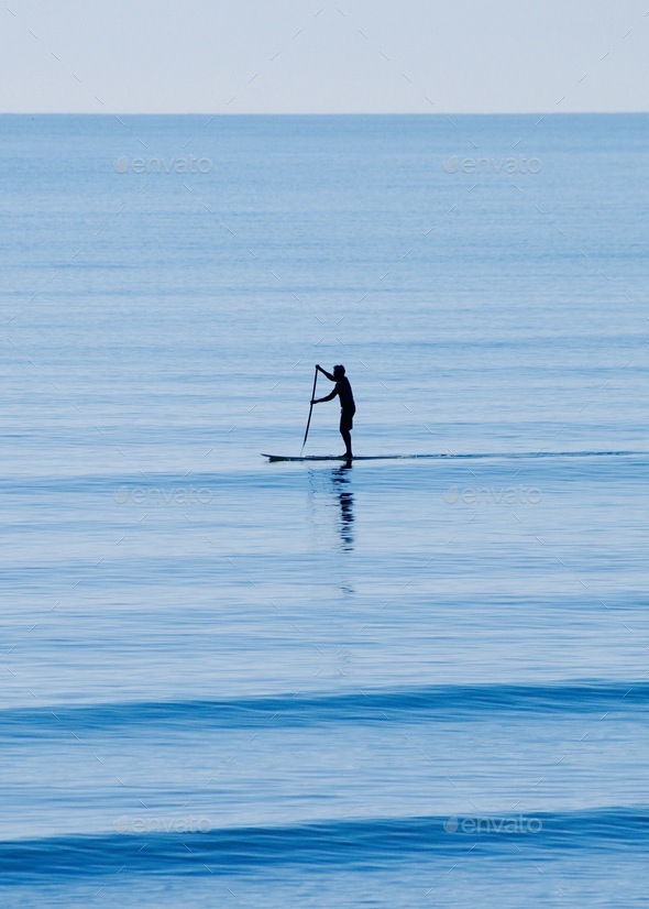 A man surfing on the calm smooth surface of the blue ocean bay Stock ...