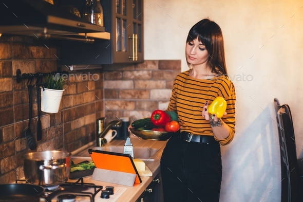 Millennial woman cooking pasta, using her tablet to read recipe on the ...