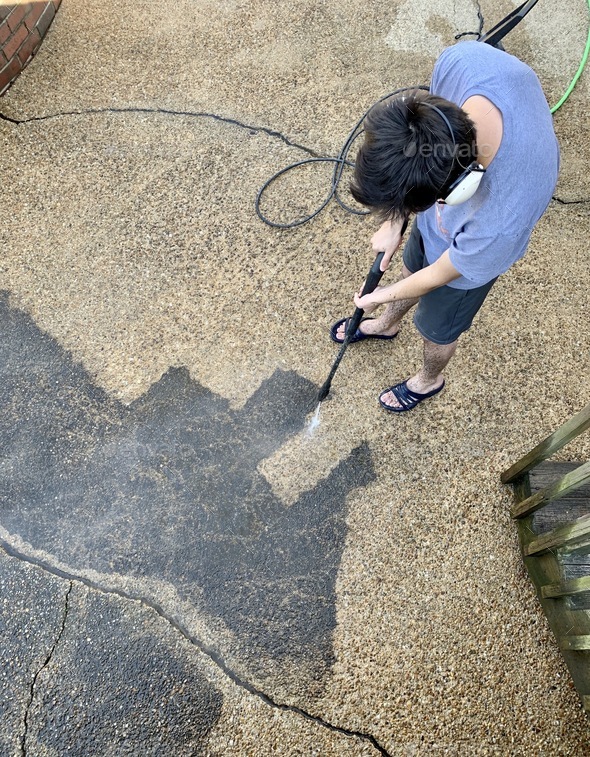 Overhead of a young GenZ adult man doing house chores power washing the ...