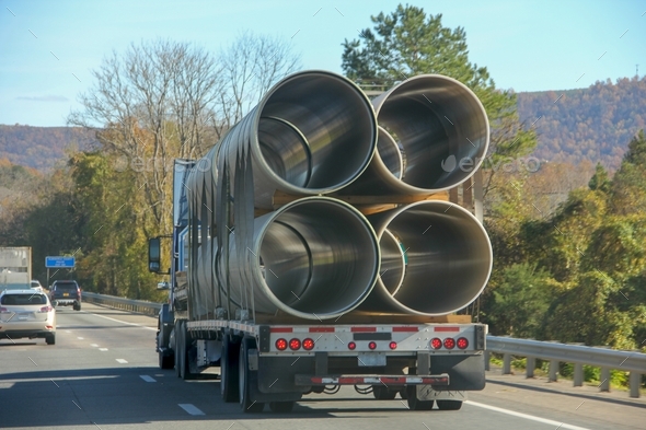 A flatbed truck carrying big size metallic cylinder pipes in the ...
