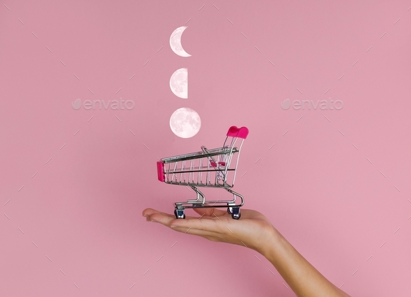 female hand holding shopping cart with moon flying into on pink ...