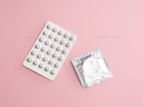 Packaging of oral contraceptives and condom on pastel pink background ...