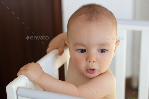 A little boy in his crib is playing and trying to get up. The child is ...