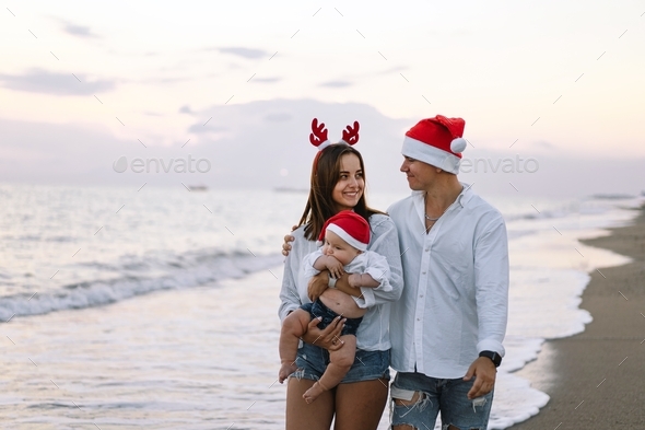 Family in a red Santa hat walk on the beach. Family celebrate Christmas ...