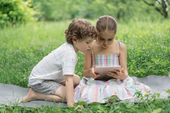 Children with a tablet outdoors. Children play games on the tablet ...