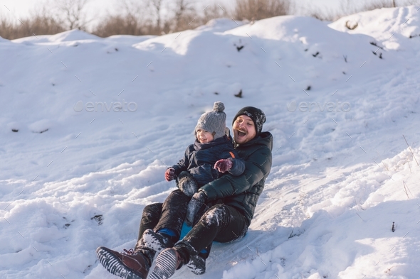 Happy dad and little boy playing with snow sled. Father and son ...