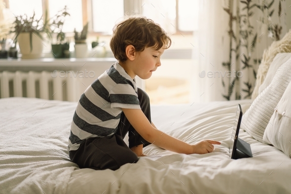 Little Boy with a tablet in the room. The boy play game on the tablet ...