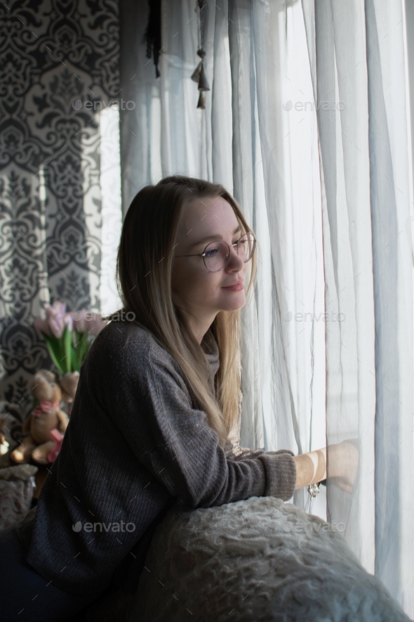 beautiful sad girl at home looking out the window Stock Photo by olgar23