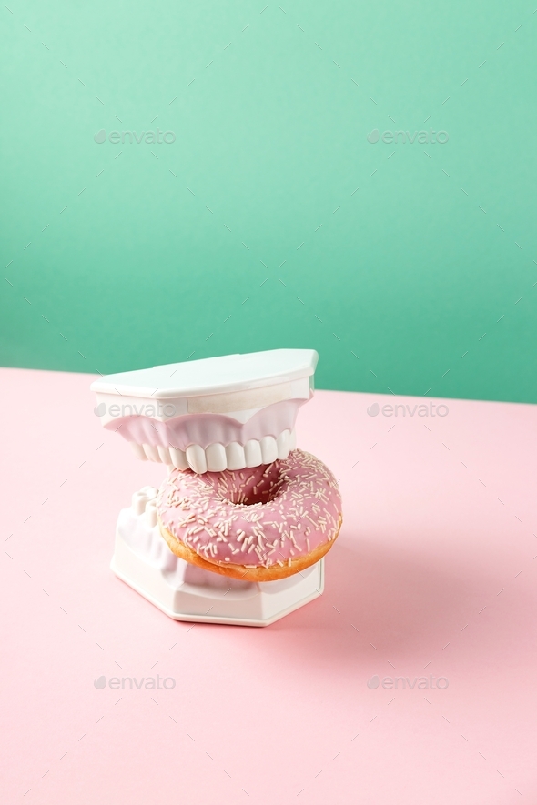 Plastic jaws hold sweet pink donut in teeth. Dental health, dentistry ...