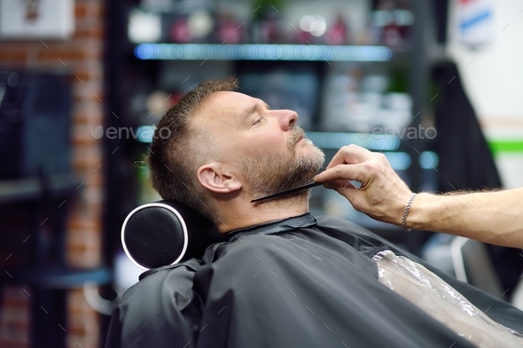 Barber master is shaving of handsome mature bearded man in salon. Hair ...