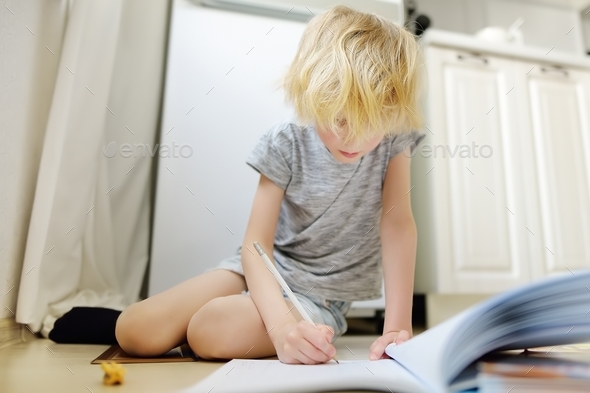Elementary student boy doing homework on floor at home. Child learning ...