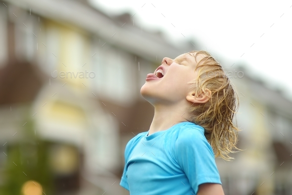 Little boy walking on rainy summer day in small town. Kid catches ...