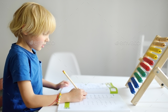 Elementary student boy doing homework at home. Child learning to count ...