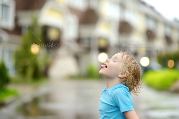 Little boy walking on rainy summer day in small town. Kid catches ...