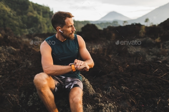 Young hipster runner with beard using smart watch and listening music ...