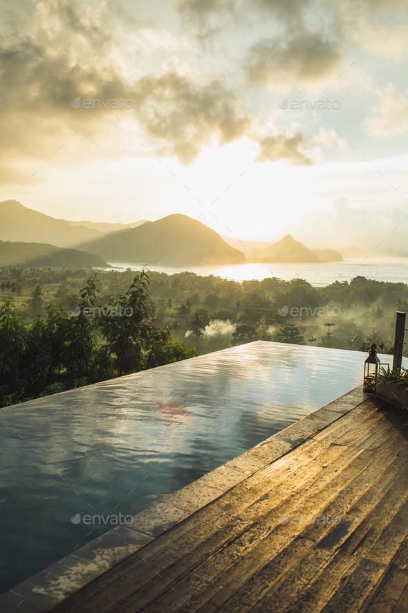 Infinity pool with amazing mountain and ocean view at sunset. Sun rays ...