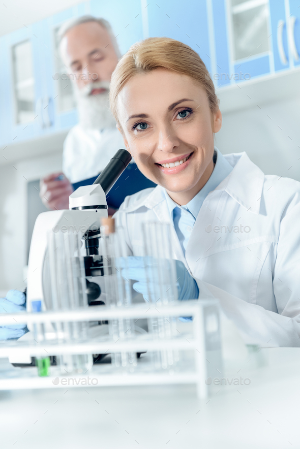 caucasian smiling scientist in white coat working with microscope and ...