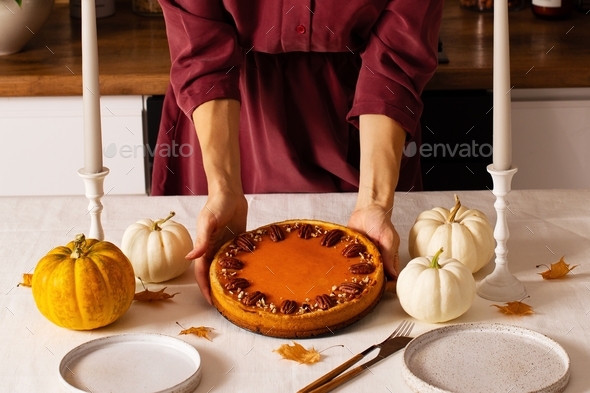 Traditional pumpkin pie on table. Woman hands putting a pie on holidays ...
