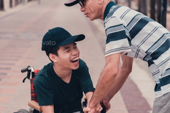 Disabled teenager boy on wheelchair funny face with carer in public ...