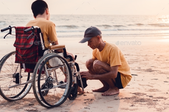 The back of a handicapped child in a wheelchair and parent on the beach ...