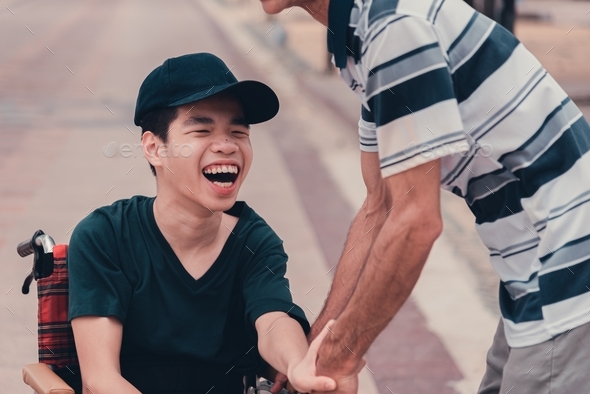 Disabled teenager boy on wheelchair funny face with carer in public ...