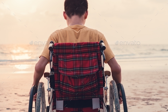 The back of a handicapped child in a wheelchair on the beach at sunset ...