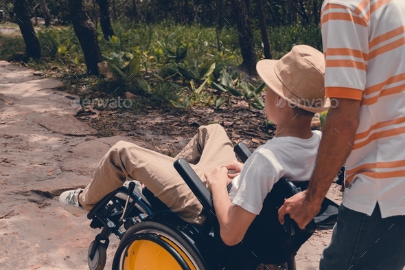 Disabled teenager boy on wheelchair and parent on the road in nature ...