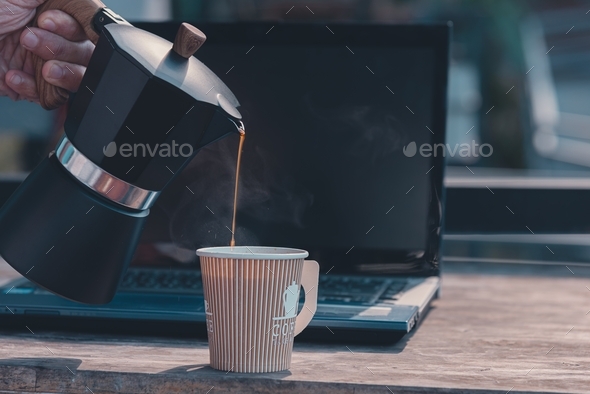 A pot of black is pouring hot coffee by hand of man into a paper cup in ...