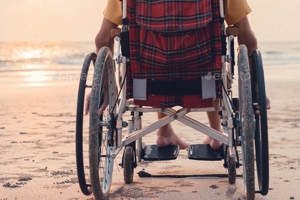 The back of a handicapped child in a wheelchair on the beach at sunset ...