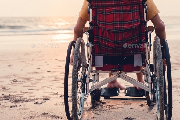 The back of a handicapped child in a wheelchair on the beach at sunset ...