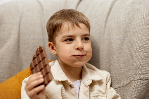Little adorable boy sitting on the couch at home and eating chocolate ...