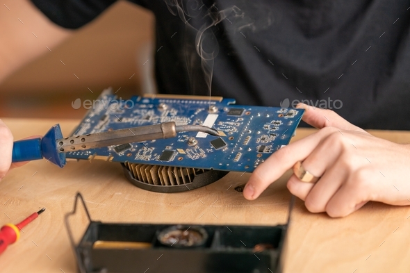 a young man solders a burnt-out microcircuit with a soldering iron ...