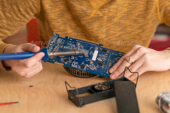 a young man solders a burnt-out microcircuit with a soldering iron ...