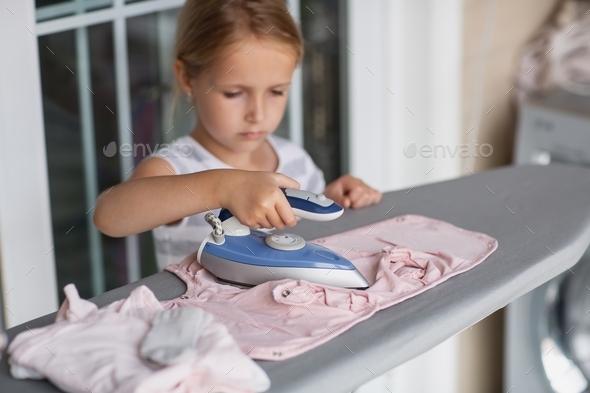Little Caucasian girl with blonde hair doing home chores and ironing ...