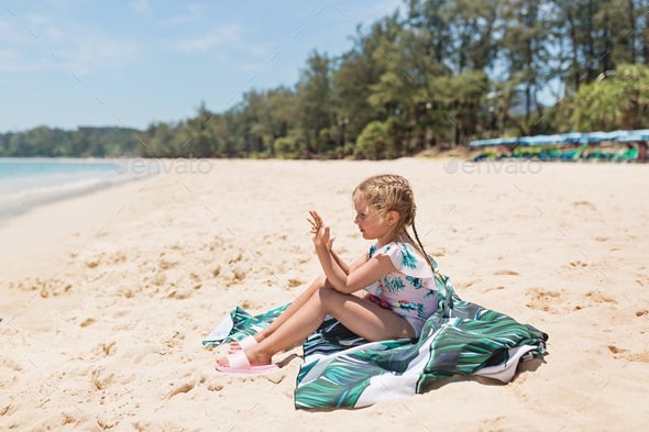 Lifestyle portrait of cute Caucasian little girl sunbathing on sandy ...